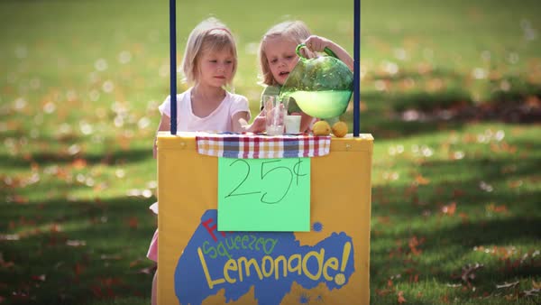 Two cute little girls get their lemonade stand ready by poring lemonade ...