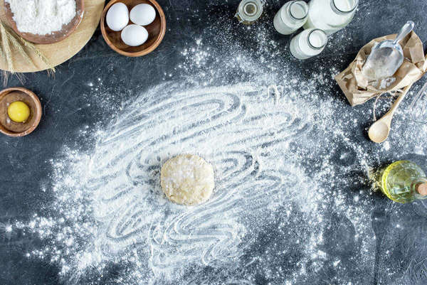 Top view of raw dough, baking ingredients and cutlery on marble surface - Stock Photo - Dissolve