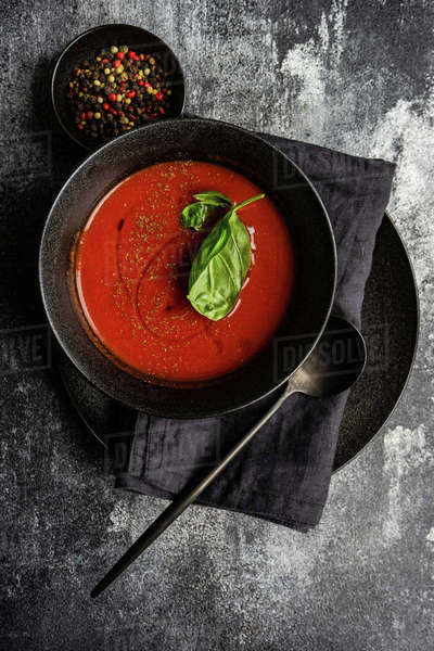 Overhead view of a bowl of gazpacho soup with basil and mixed peppercorns - Stock Photo - Dissolve