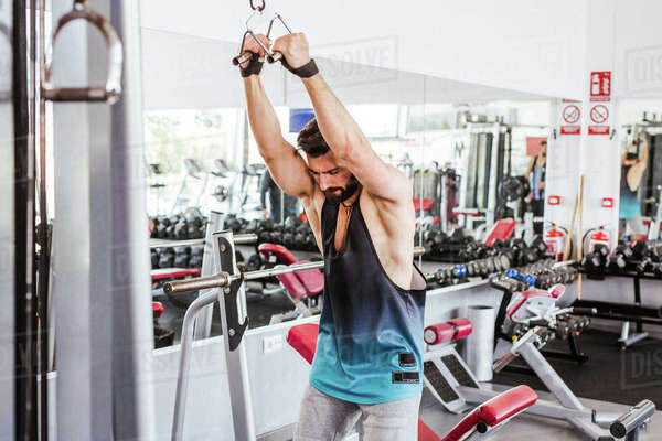 Powerful determined sportsman doing exercise with barbell at squat rack during weightlifting ...