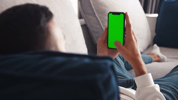 Man lying on couch using smartphone with chroma key green screen , scrolling various gestures ...