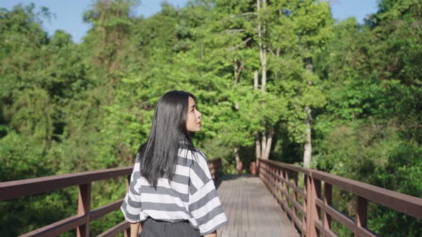Asian young woman enjoying a surrounding view while walking on a wooden bridge inside national ...