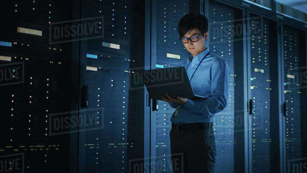 In Dark Data Center: Male IT Specialist Walks along the Row of Operational Server Racks, Uses ...