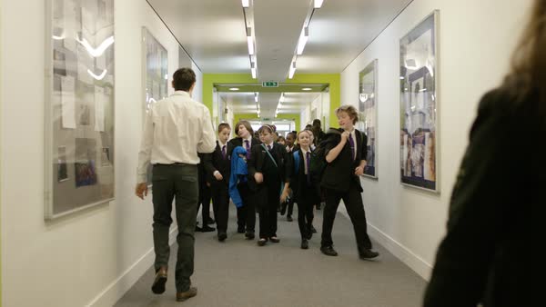 Teachers & young students chatting & walking through busy school ...