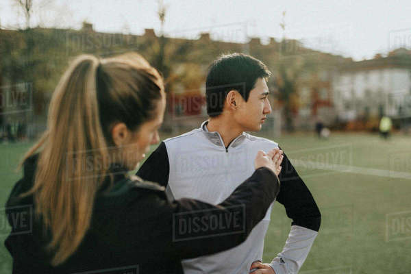 Female coach talking with male athlete while standing in sports field - Stock Photo - Dissolve