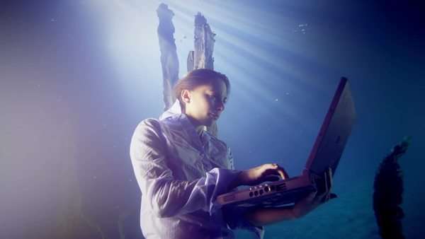 Underwater businesswoman working on a laptop computer in deep blue ...
