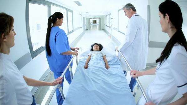 Wide angle view child patient taken on hospital bed by male female ...