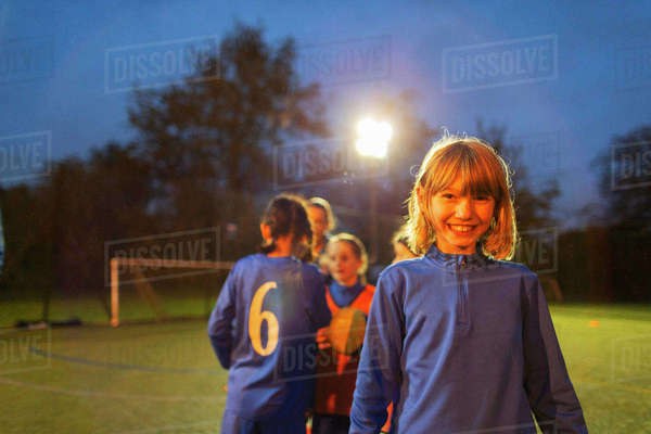 Portrait confident girl playing soccer with team on field at night ...