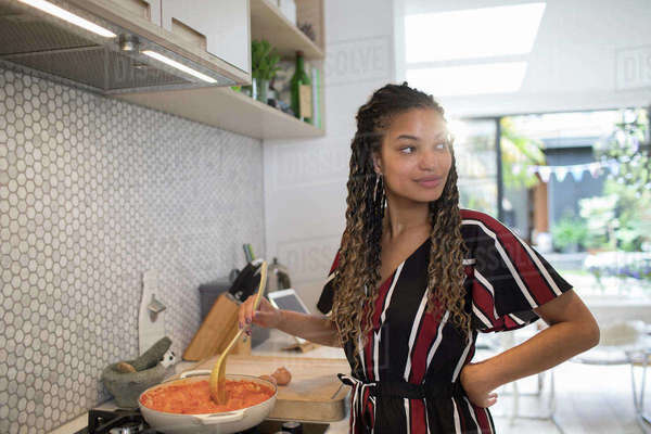 Young woman cooking at stove in kitchen - Stock Photo - Dissolve
