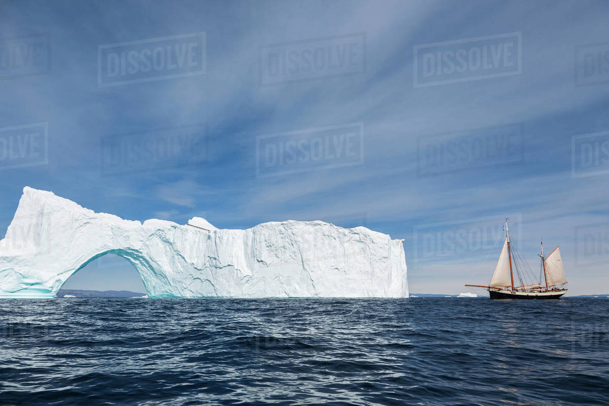 Ship sailing toward sunny majestic iceberg with arch Greenland ...