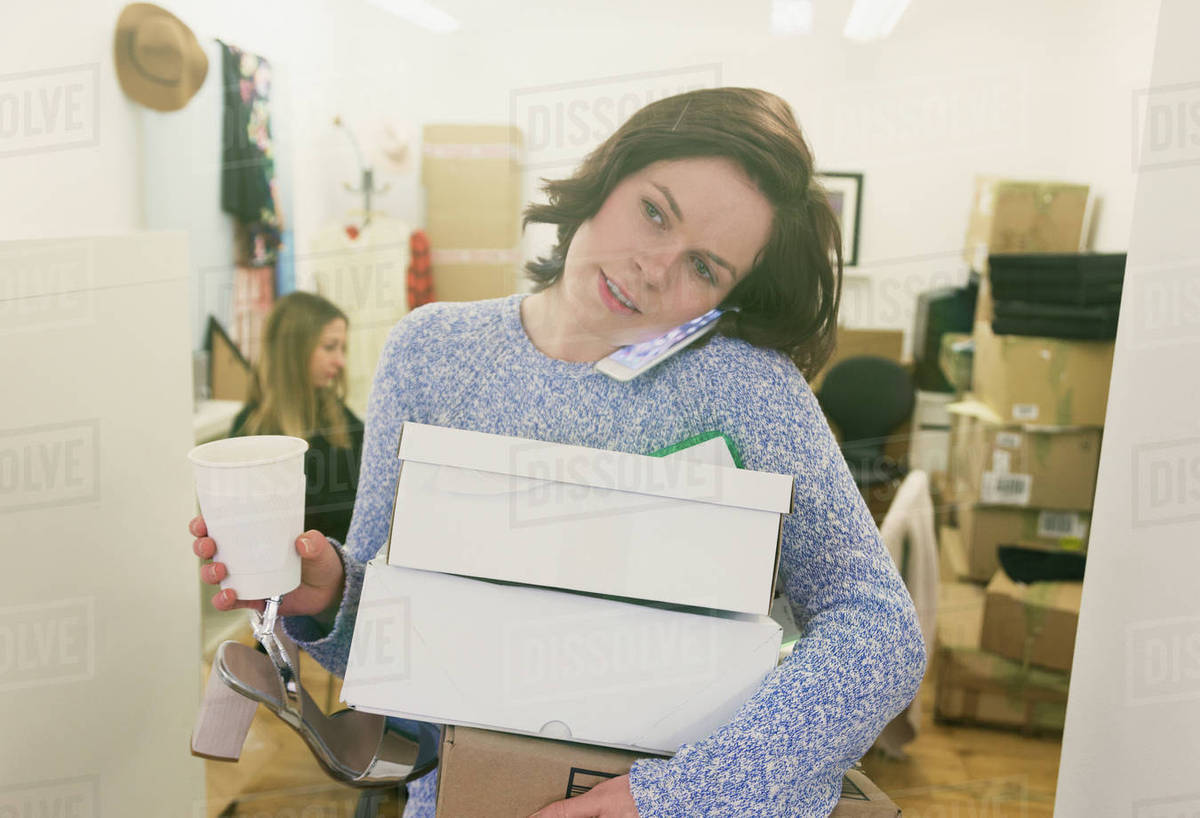 Fashion buyer multitasking carrying shoe boxes, coffee and talking on ...