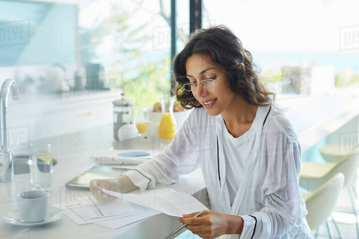 Businesswoman in bathrobe working reviewing paperwork at kitchen ...