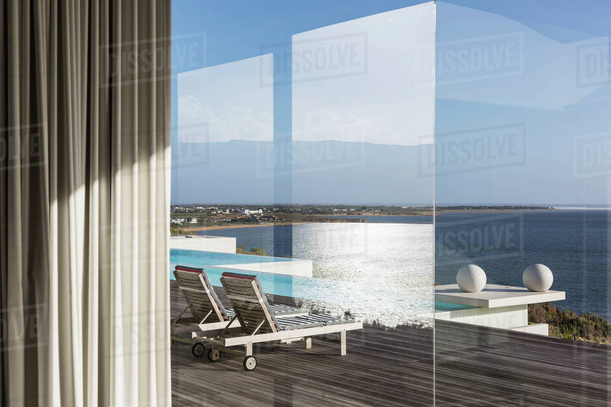 Window view of sunny modern luxury patio with infinity pool and ocean ...