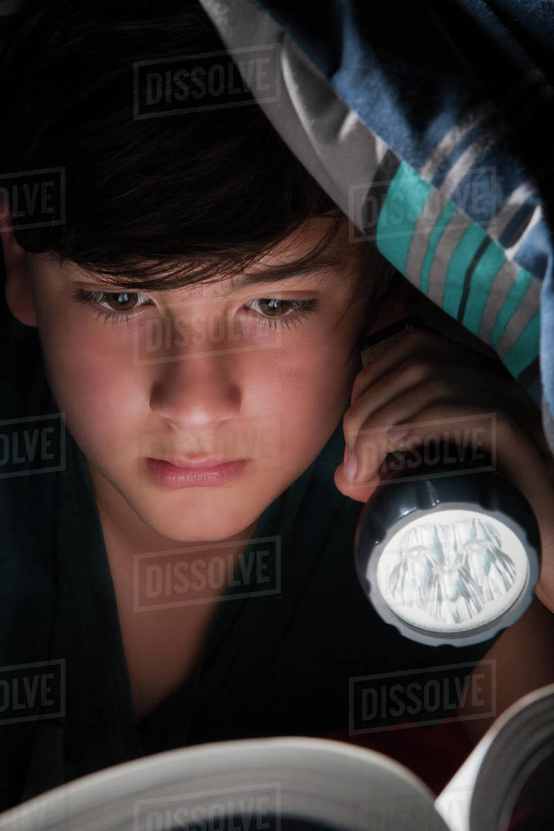 Boy reading with torch under blanket - Stock Photo - Dissolve