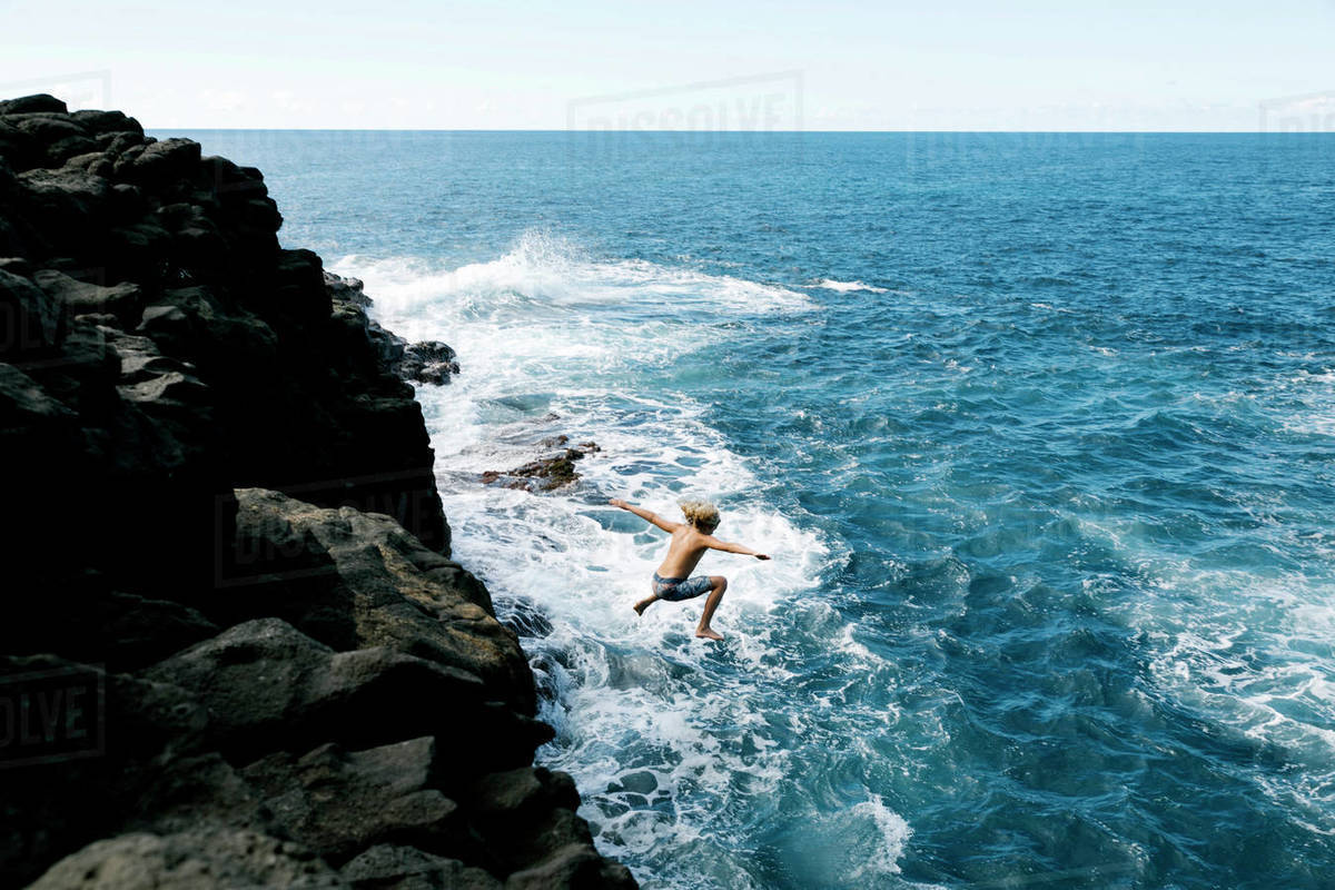 Boy jumping off cliff by sea - Royalty-free Stock Photo | Dissolve