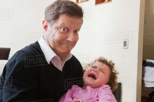 Father making face while holding crying daughter - Stock Photo - Dissolve