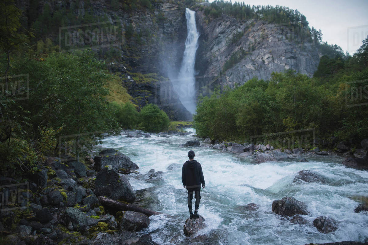 Young man standing by waterfall - Stock Photo - Dissolve