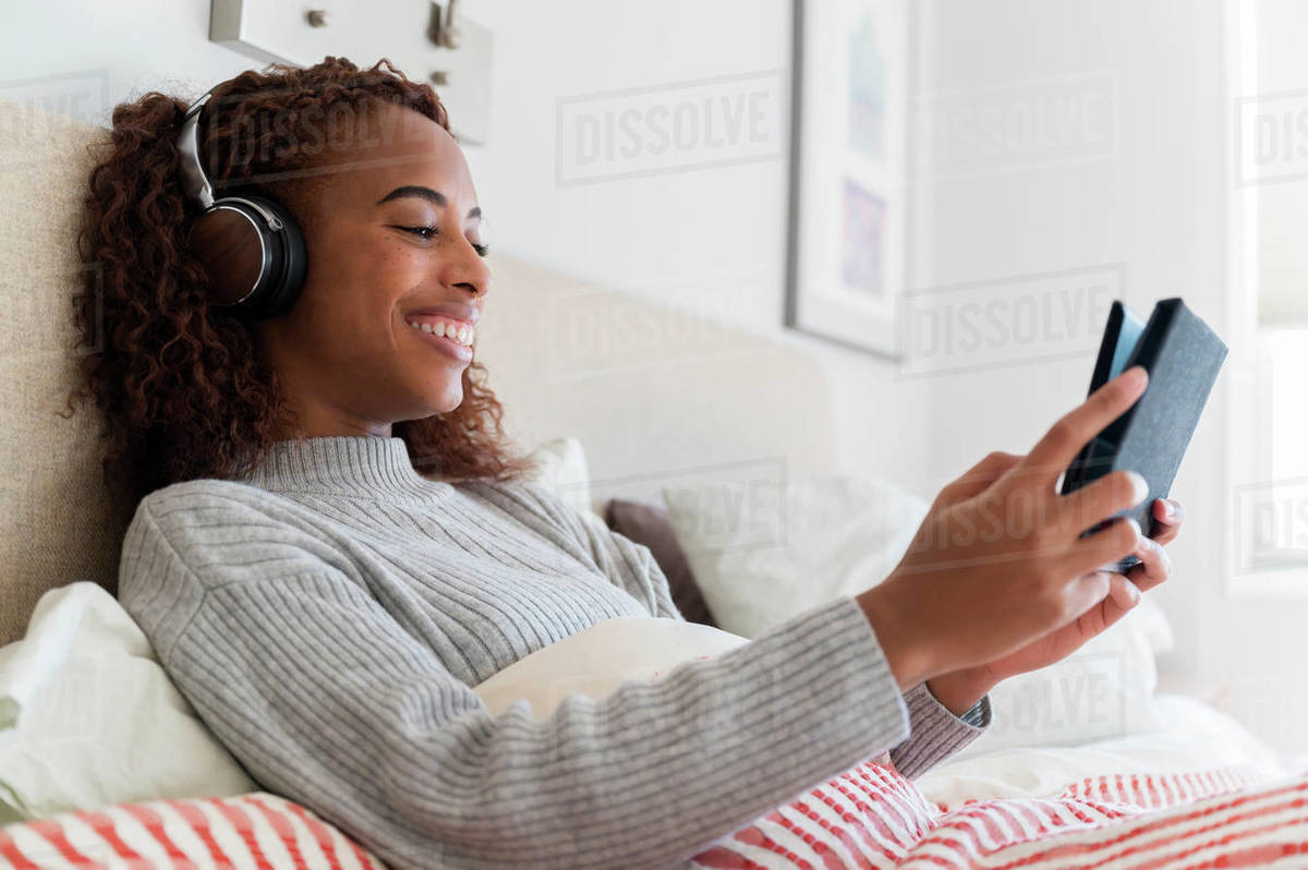 Smiling woman using tablet with headphones in bed - Royalty-free Stock ...