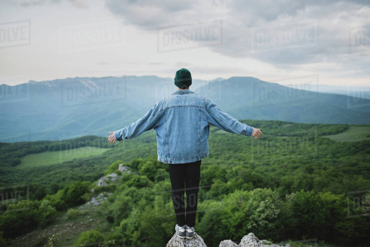 Man standing on cliff by mountain and forest - Royalty-free Stock Photo ...