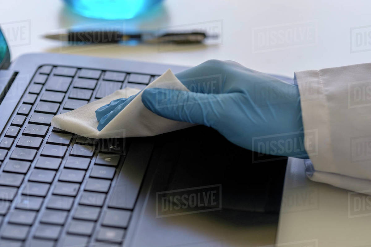 Person wearing blue surgical glove cleaning keyboard of laptop ...