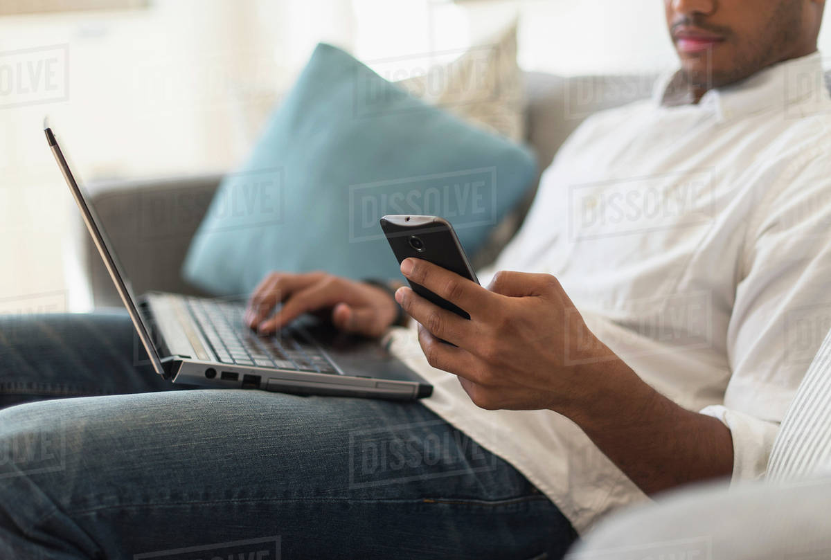 Man sitting in living room, using laptop and cell phone - Royalty-free ...