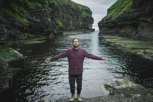 Denmark, Faroe Islands, Gjogv, Man standing inn gorge with outstretched ...