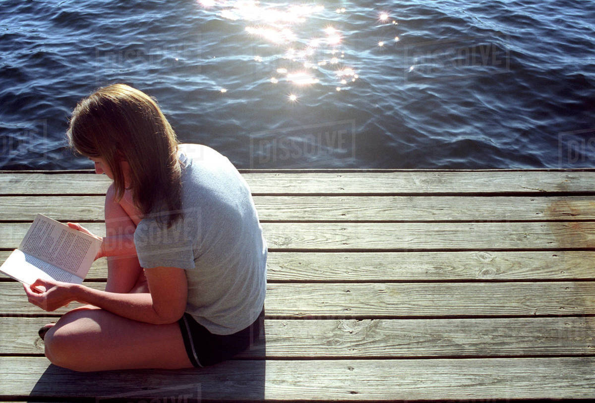 Woman reading on dock by lake - Stock Photo - Dissolve