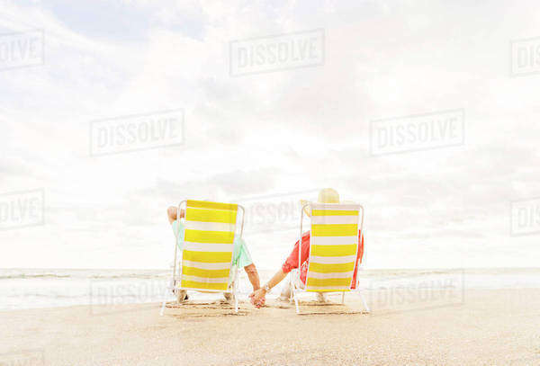 Rear view of couple sitting in lounge chairs on beach - Royalty-free ...