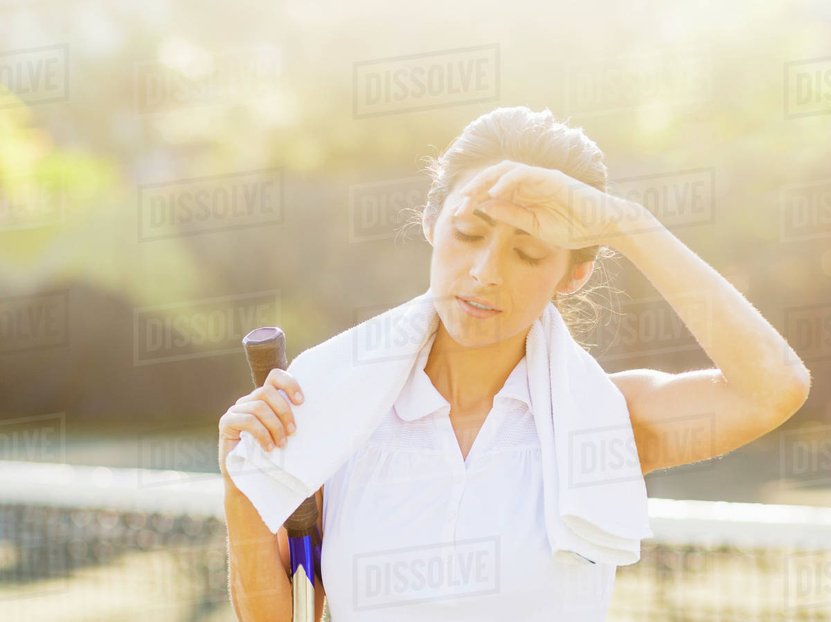 Portrait of young woman with towel and tennis racket wiping forehead ...