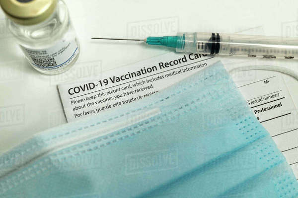 Syringe on Covid-19 vaccination record card, face mask and vial ...