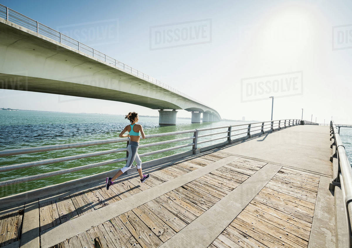 Rear view of woman jogging on bridge on sunny day - Royalty-free Stock ...