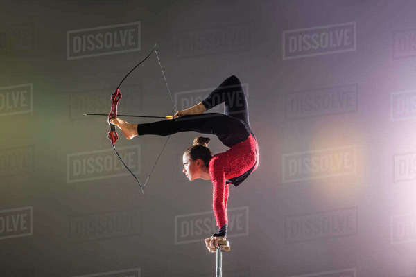 Young acrobat performing with archery bow on gymnastics bar - Royalty ...