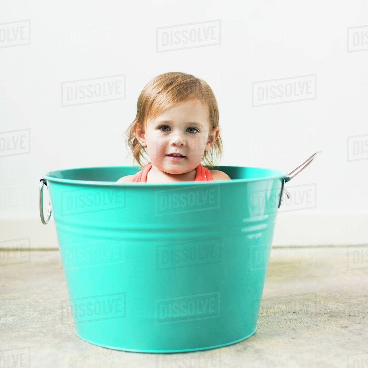 Little girl (2-3) sitting in turquoise bucket - Stock Photo - Dissolve