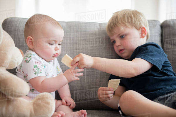 Brother (2-3) sharing crackers with baby sister (12-17 months ...