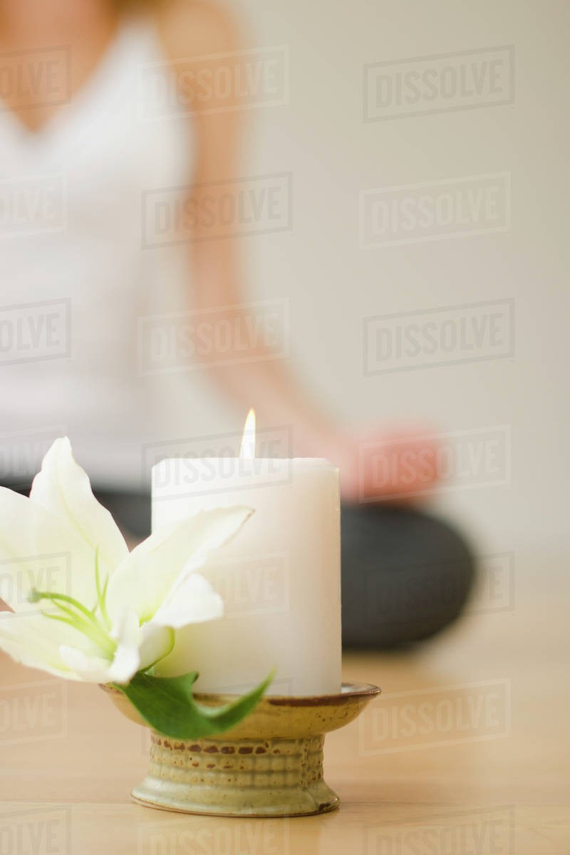 Candle and flower with woman practicing yoga in background, studio shot ...