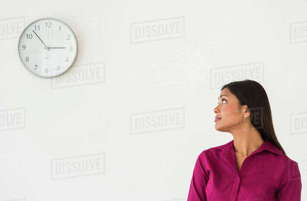 Woman looking at clock on wall - Royalty-free Stock Photo | Dissolve