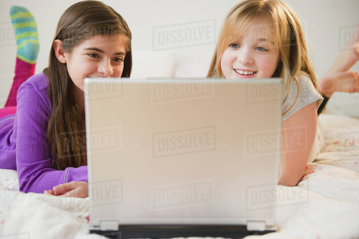 Two girls using laptop on bed - Stock Photo - Dissolve