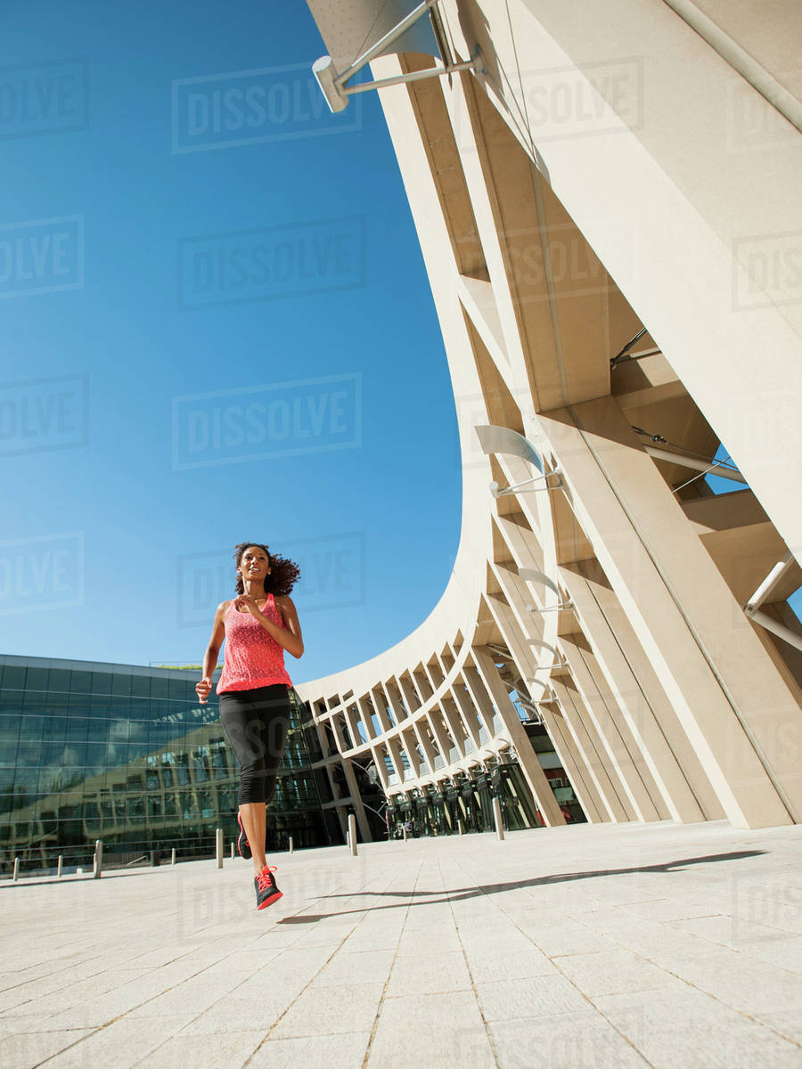 Young woman jogging along modern building - Stock Photo - Dissolve
