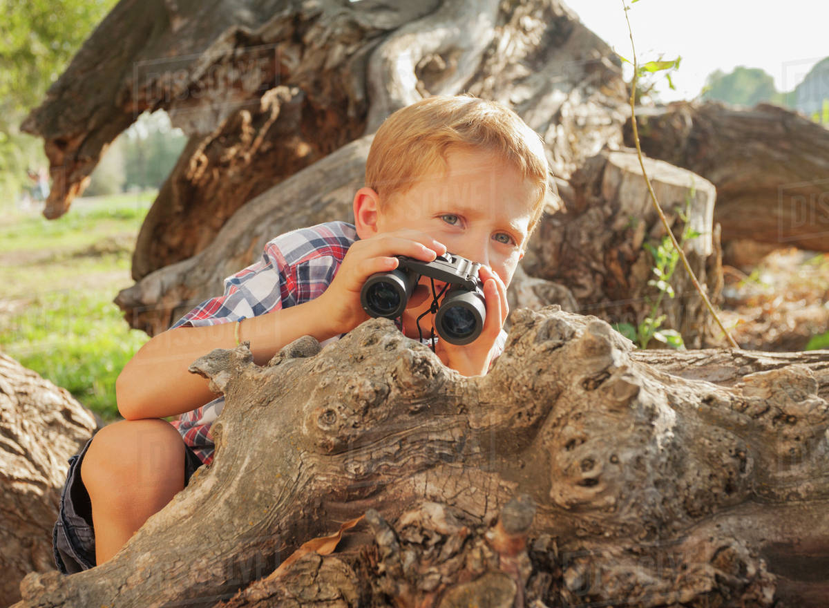 Little boy (6-7) looking at something in the distance with binoculars ...