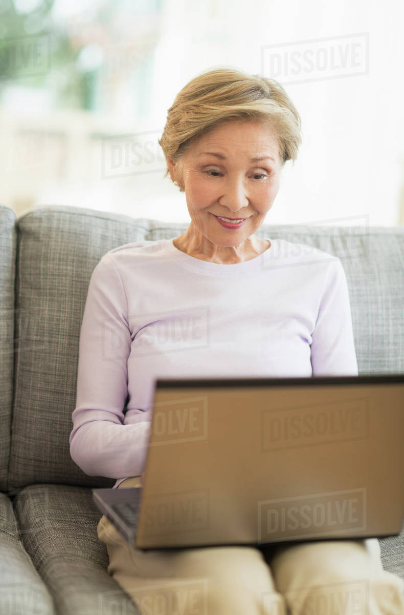 Senior woman sitting on sofa and using laptop - Royalty-free Stock ...