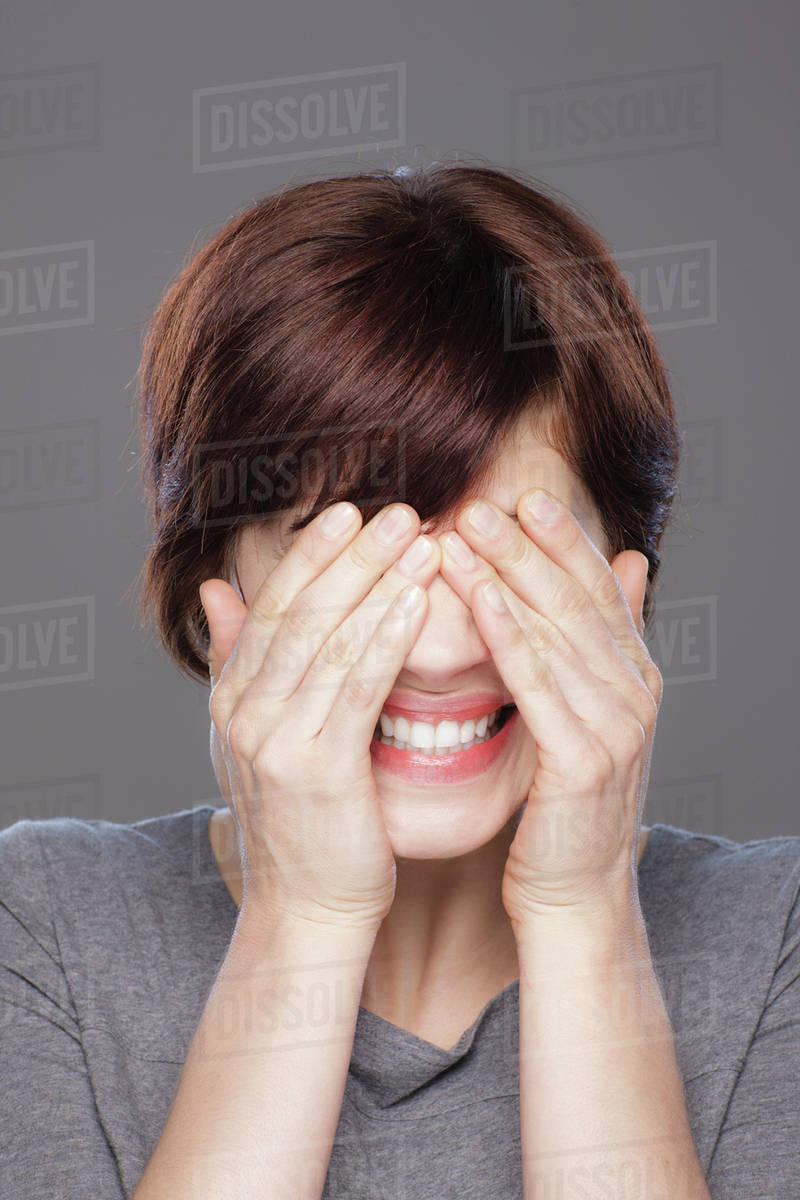 Studio shot of young smiling woman covering face with hands - Royalty ...