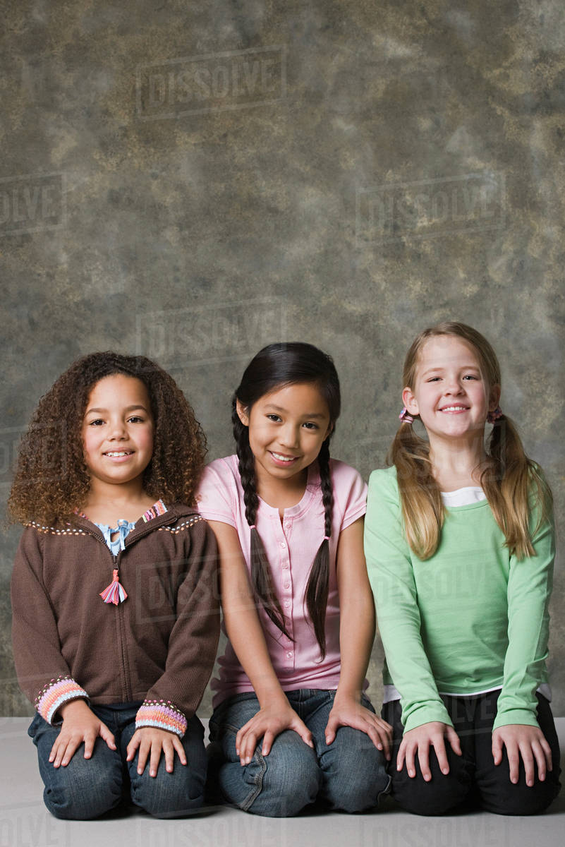 Portrait of three smiling girls (8-9) sitting together, studio shot ...