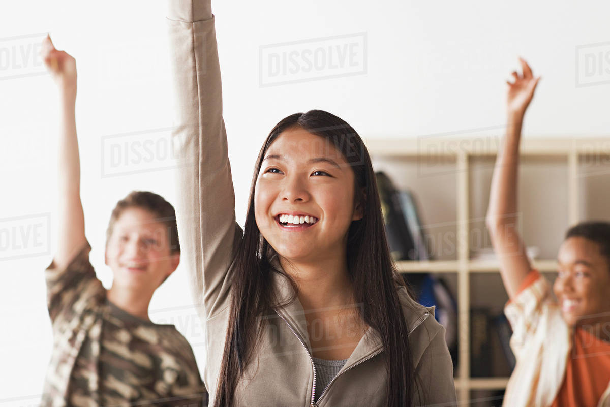 School children rising hands in classroom - Stock Photo - Dissolve