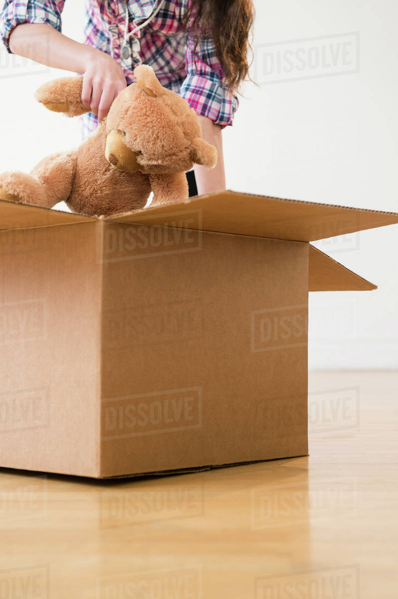Girl (8-9) packing teddy bear to carton box - Stock Photo - Dissolve