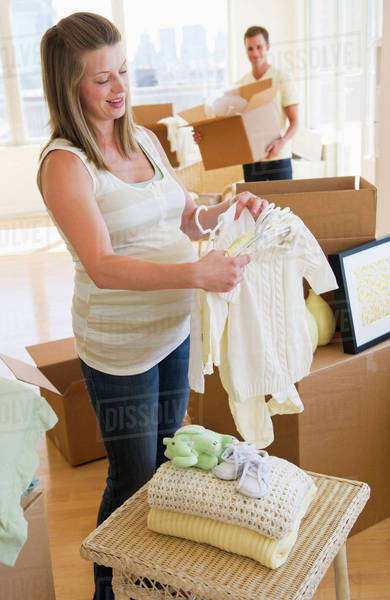 Young couple unpacking baby clothing - Stock Photo - Dissolve