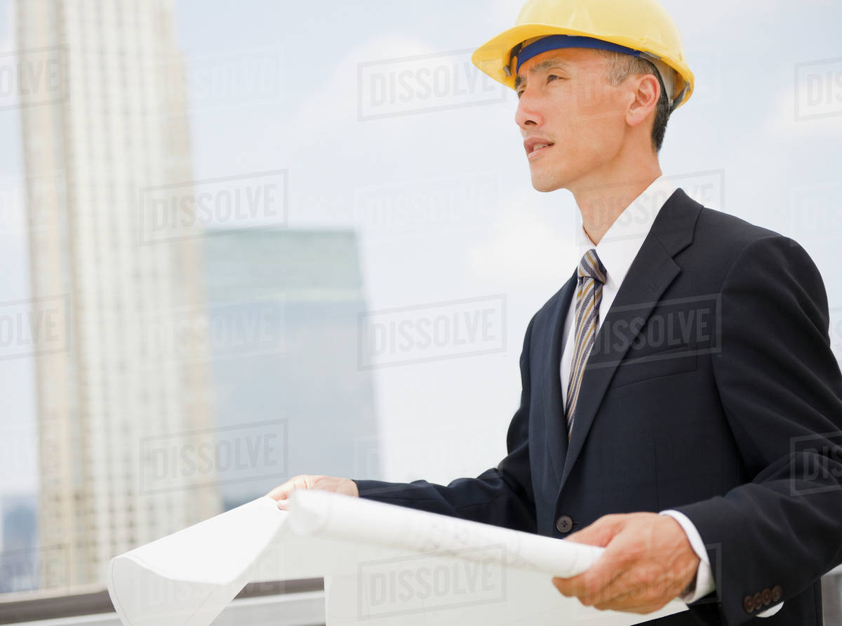 Engineer holding plans, wearing protective helmet and looking away ...