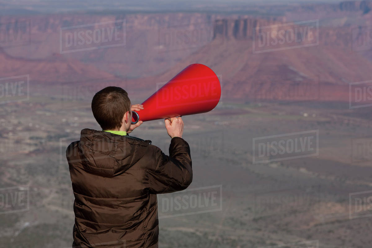 Man using megaphone at top of canyon - Royalty-free Stock Photo | Dissolve