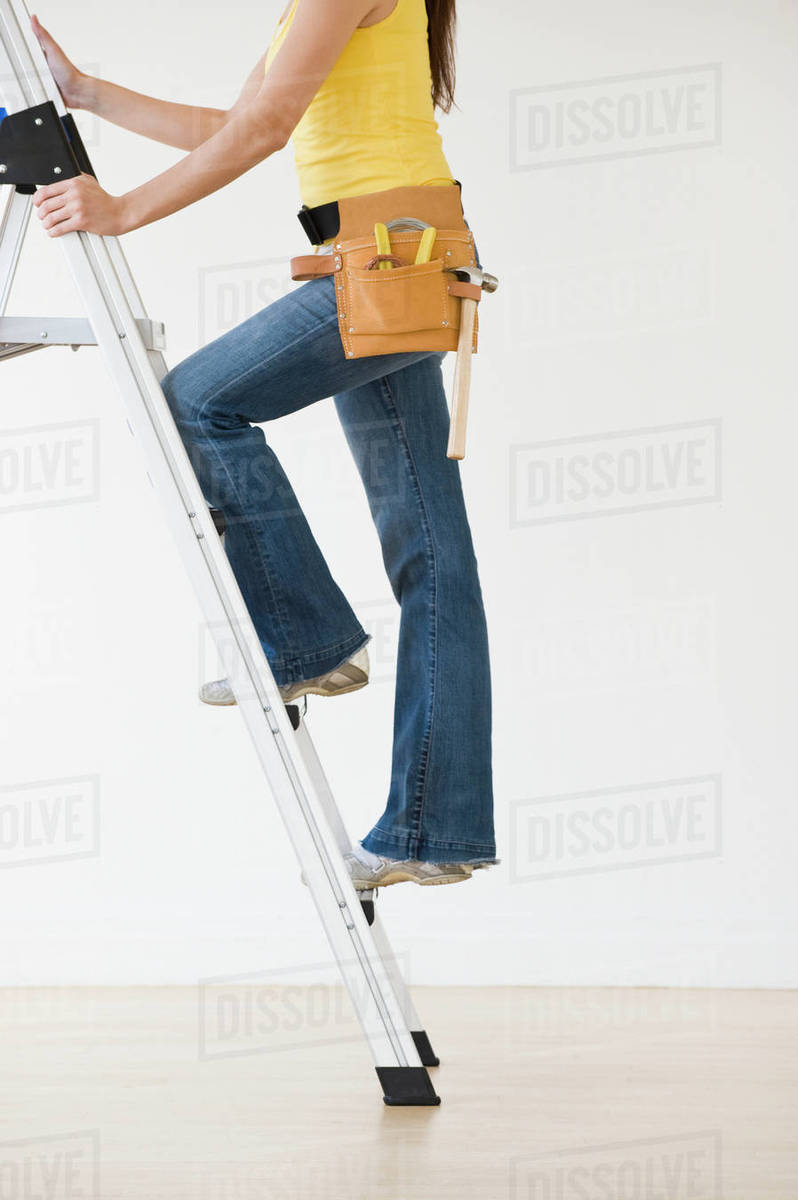 Woman wearing tool belt climbing ladder - Royalty-free Stock Photo ...