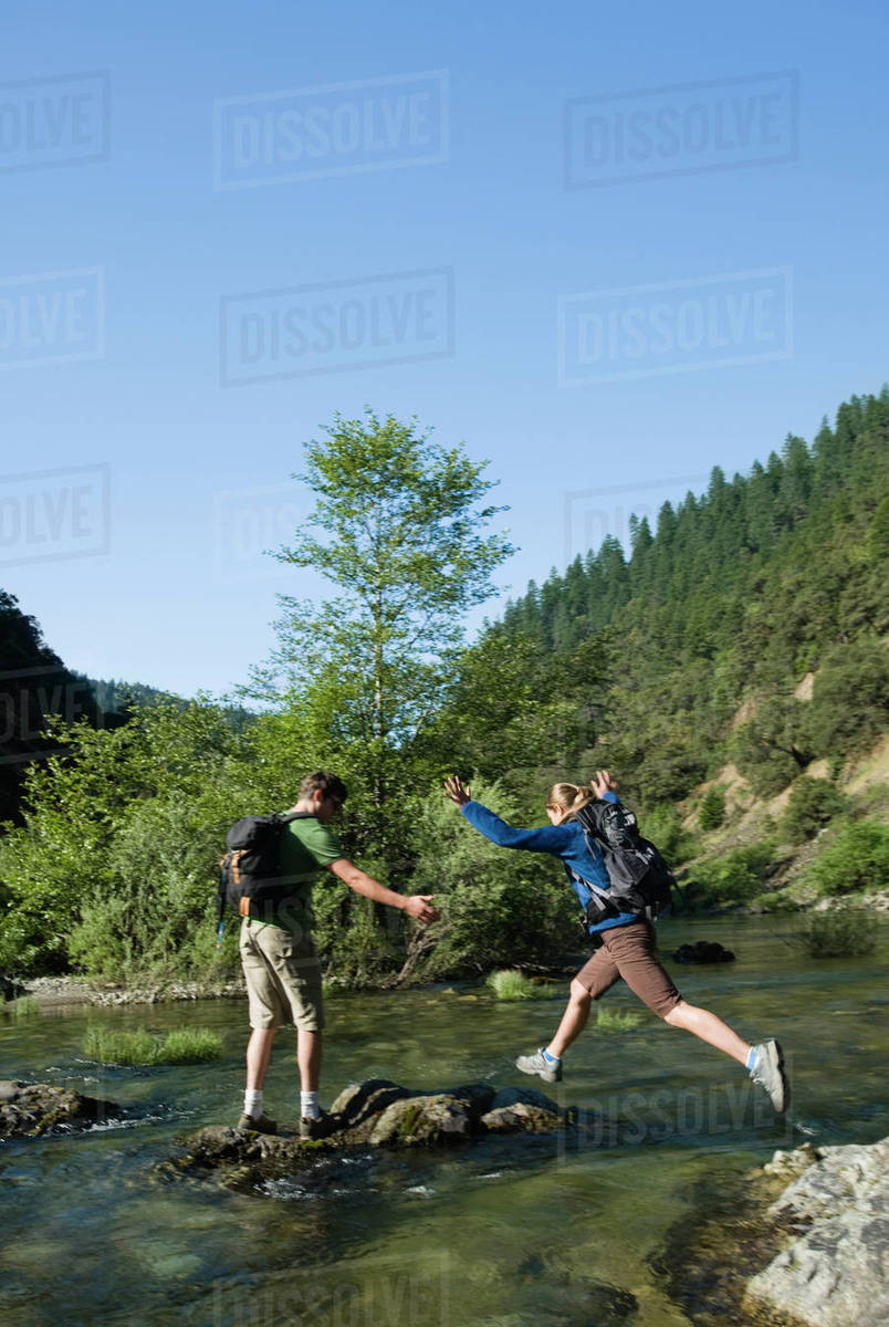 Hikers jumping across river on rocks - Stock Photo - Dissolve