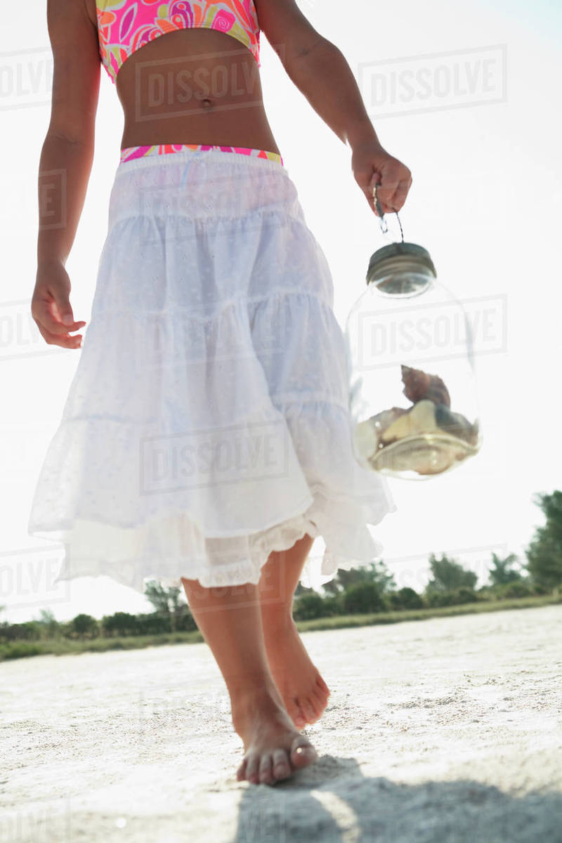 Girl on beach carrying jar of shells - Royalty-free Stock Photo | Dissolve